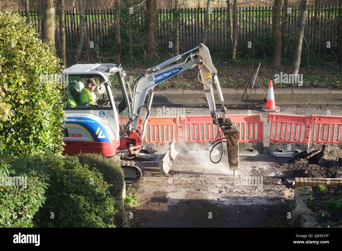 Workman using a mini excavator to dig up a pavement (sidewalk) by a ...