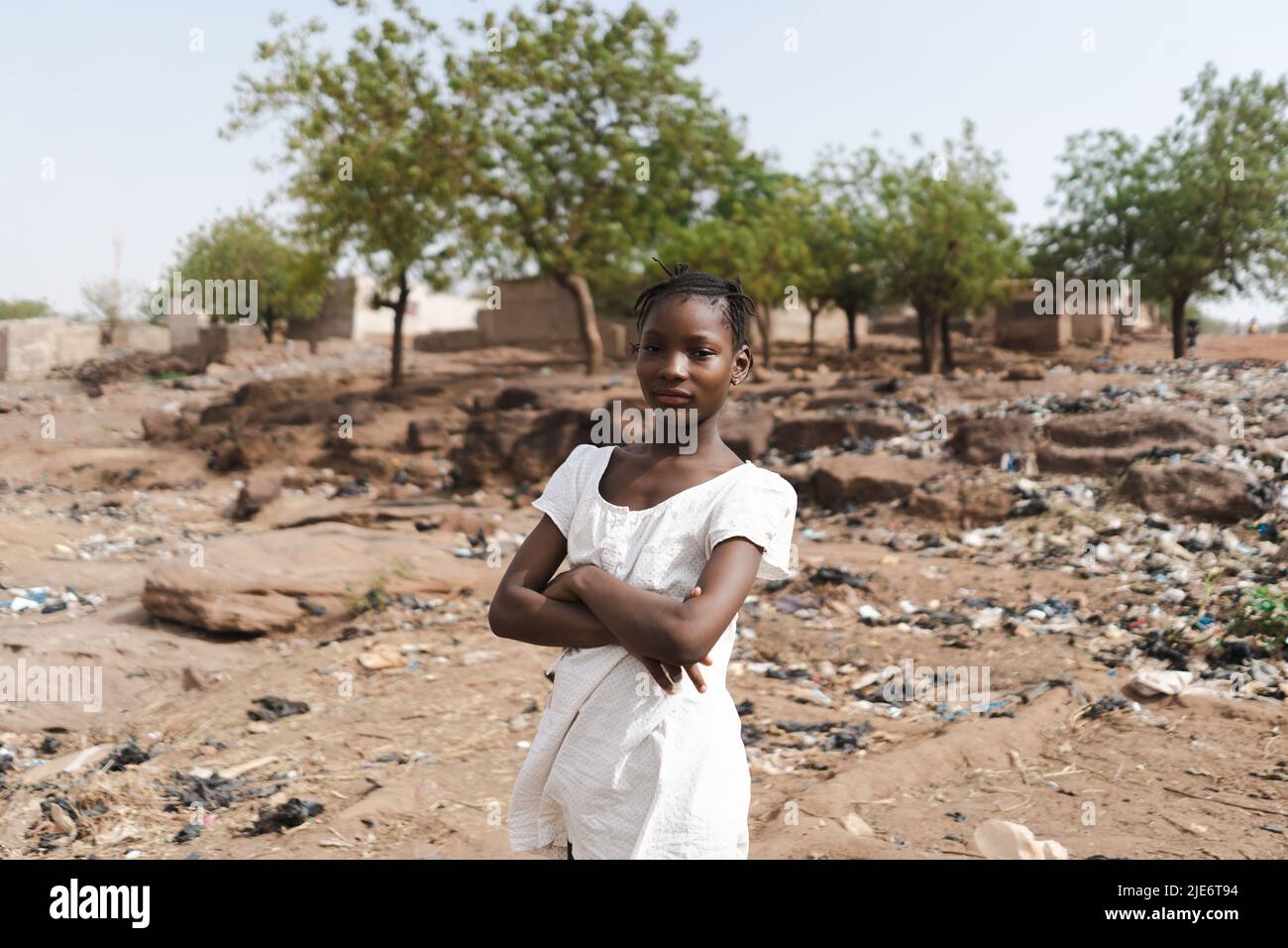 Serious African girl standing on the outskirts of her village ...