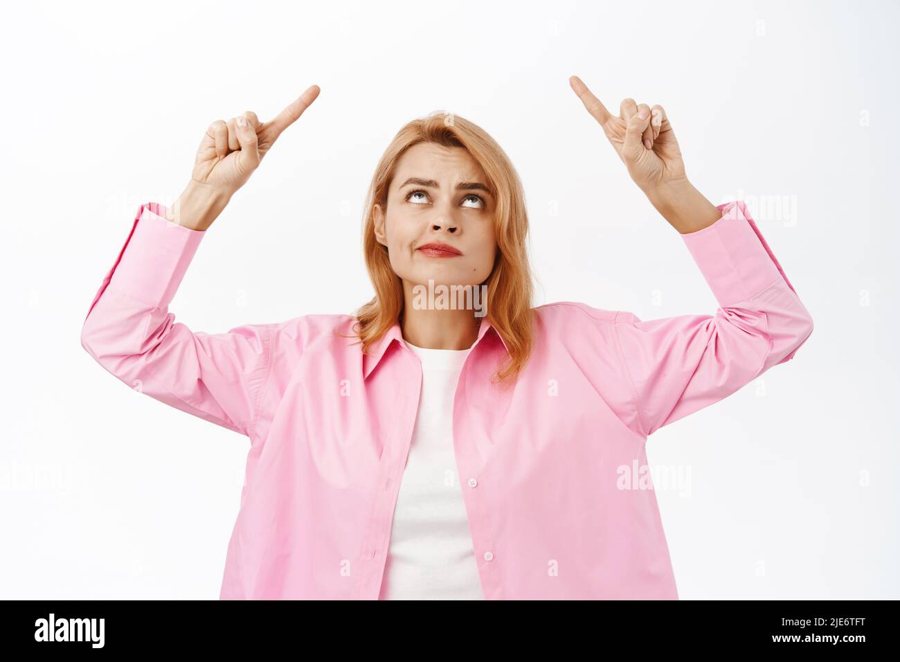 Complicated girl looks uneasy and points up, showing smth on top with ...