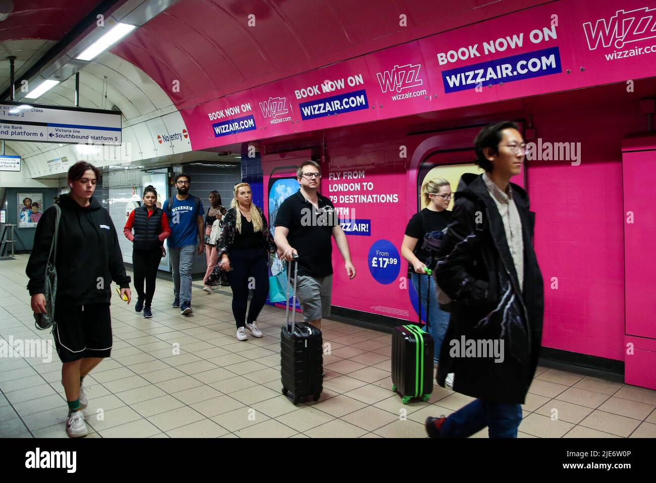 Passengers with suitcases walk past Wizz Air advert displayed at a tube ...