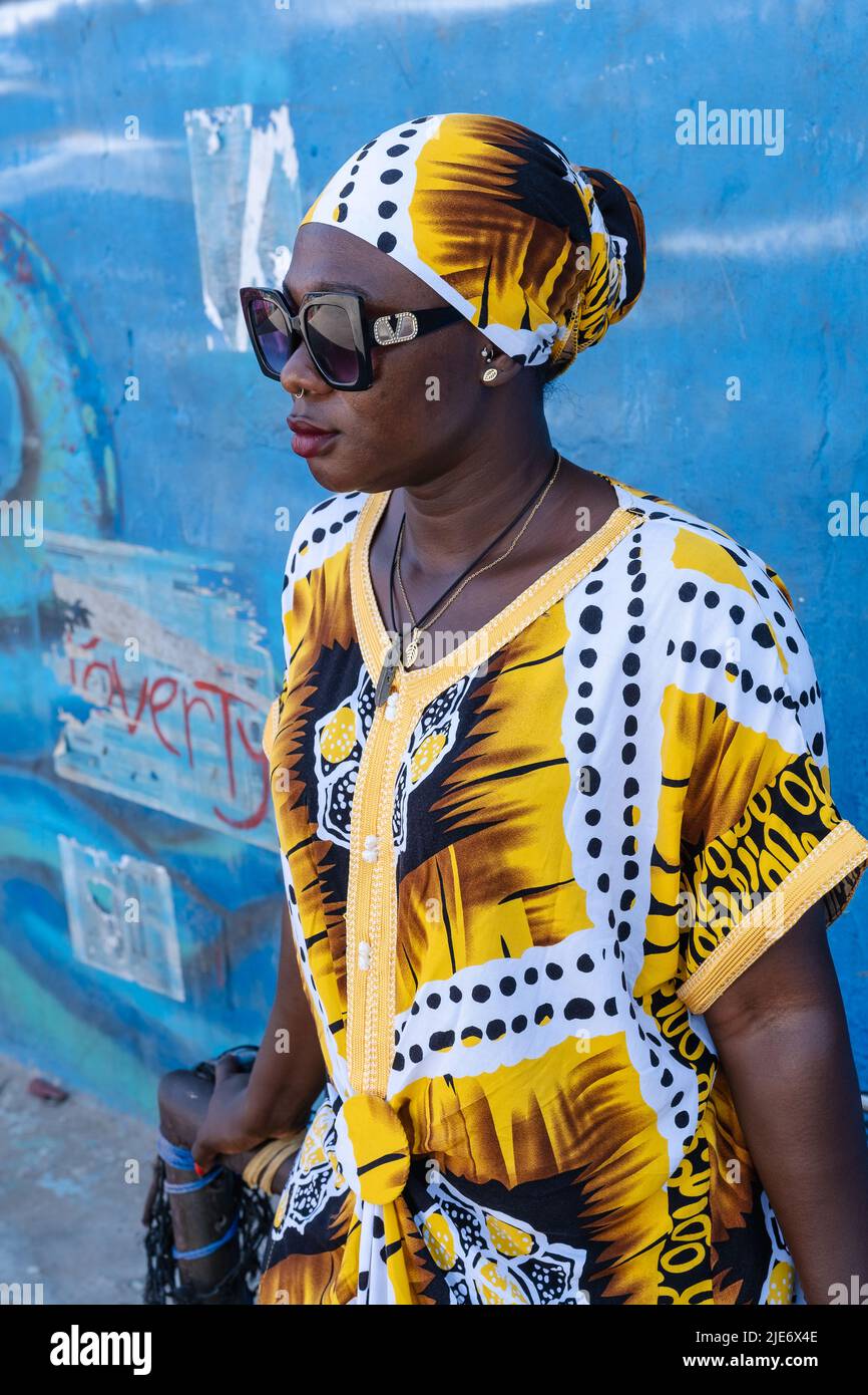 African woman in colorful suit and headdress stands in a backyard in ...