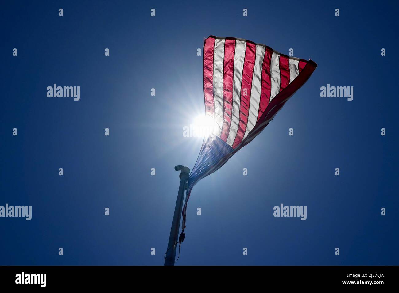 A low angle view of an American flag back lit by the sun blowing in the ...