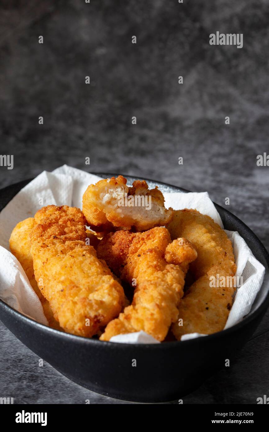 Breaded chicken fillet strips on a paper towel in a black bowl. On a ...