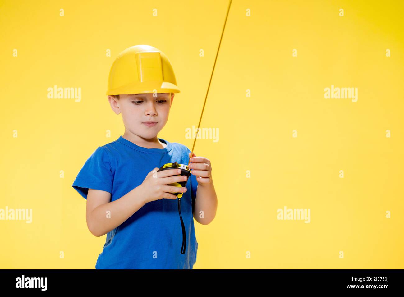 A little boy in a protective construction helmet measures with a tape ...