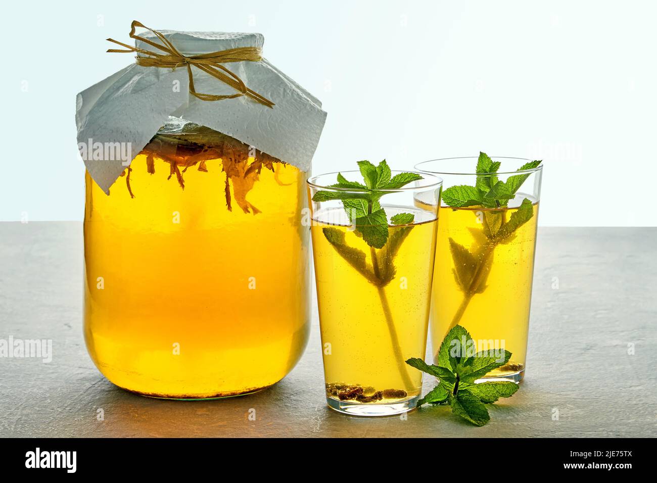 Jar of kombucha and two glass glasses of kombucha are garnished with ...
