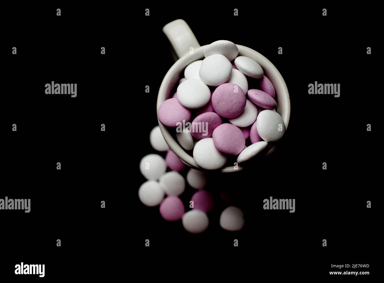 Pink and white peppermint candies in a white cup on a black background ...