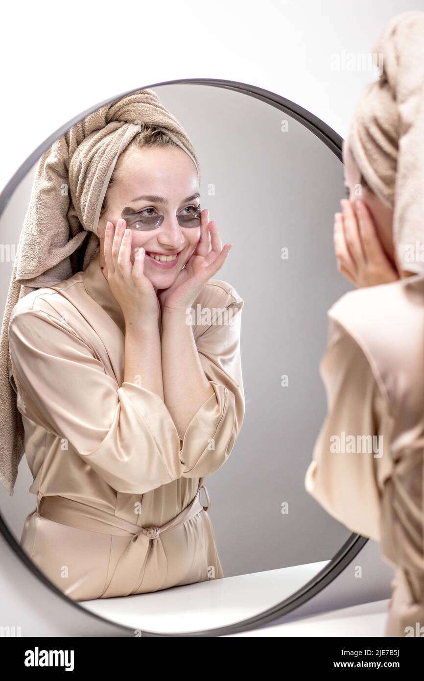 A Well Groomed Woman At Home In A Bathrobe And Towel Applies Patches