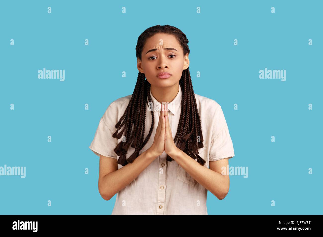 Cute woman with dreadlocks keeps palms pressed together, pleading angel ...