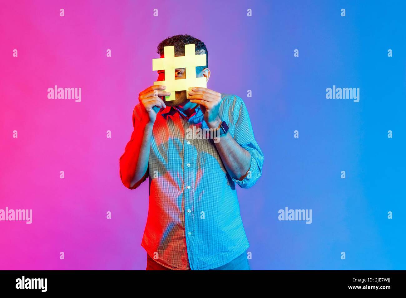 Portrait of young adult man in shirt looking through big hashtag symbol ...