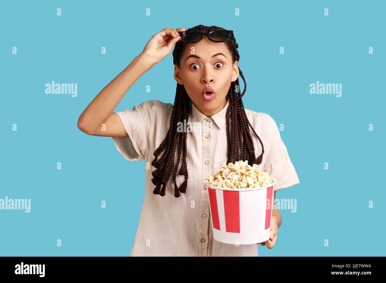 Excited woman with black dreadlocks holding bucket popcorn and raising ...