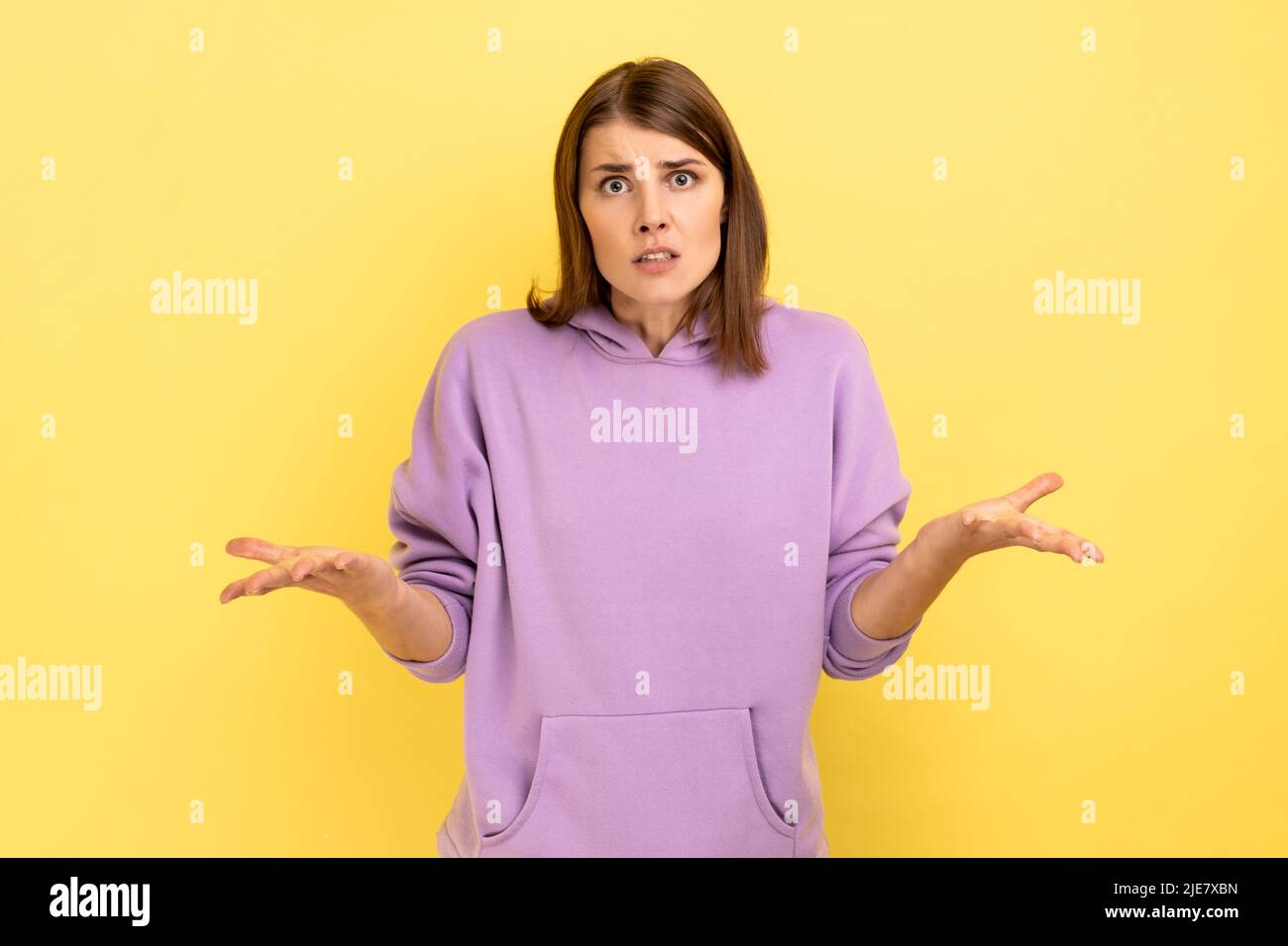 Portrait of dark haired woman raising hands and looking with confused ...