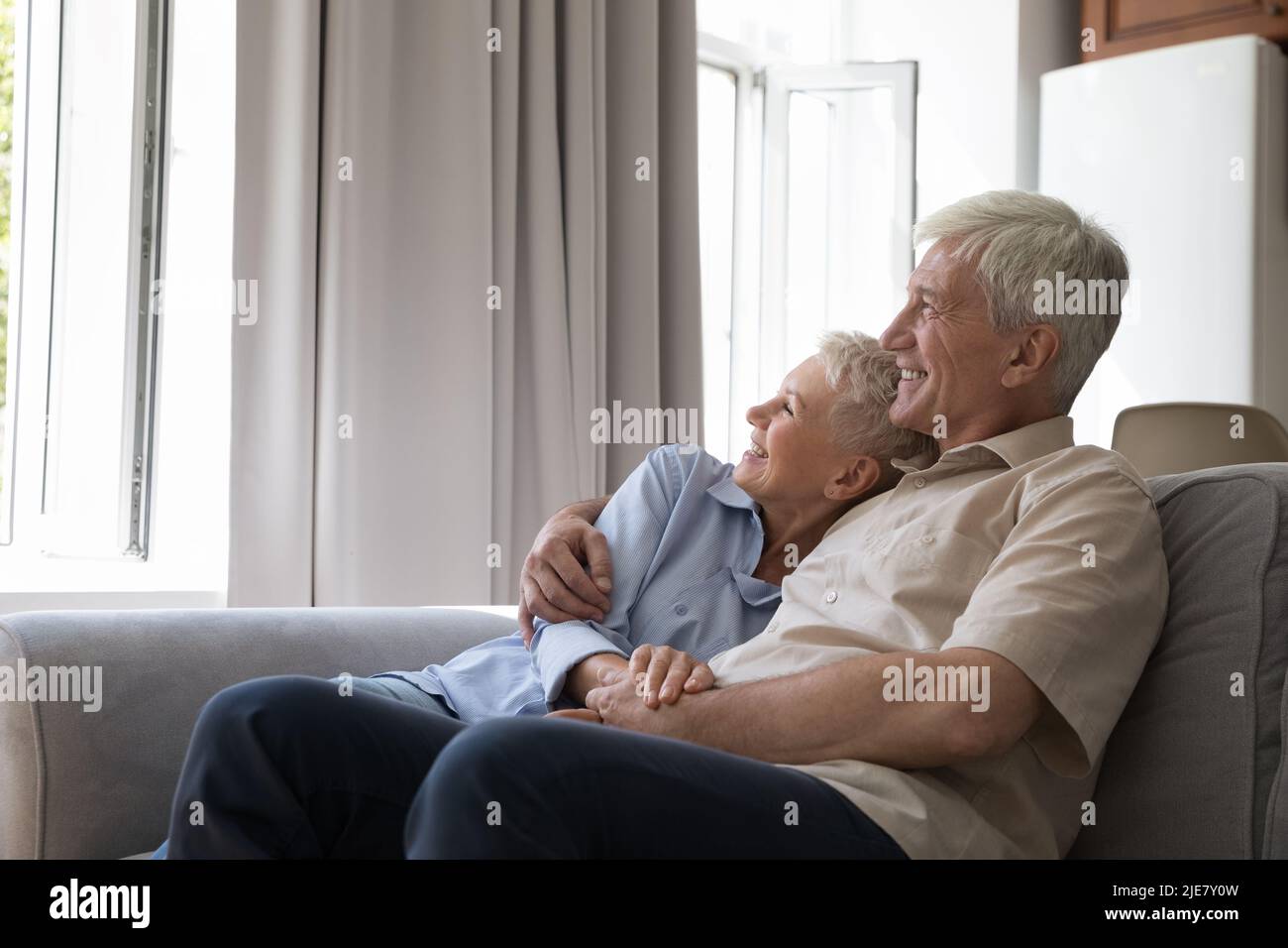Laughing older couple in love hugging daydreaming relaxing on sofa ...