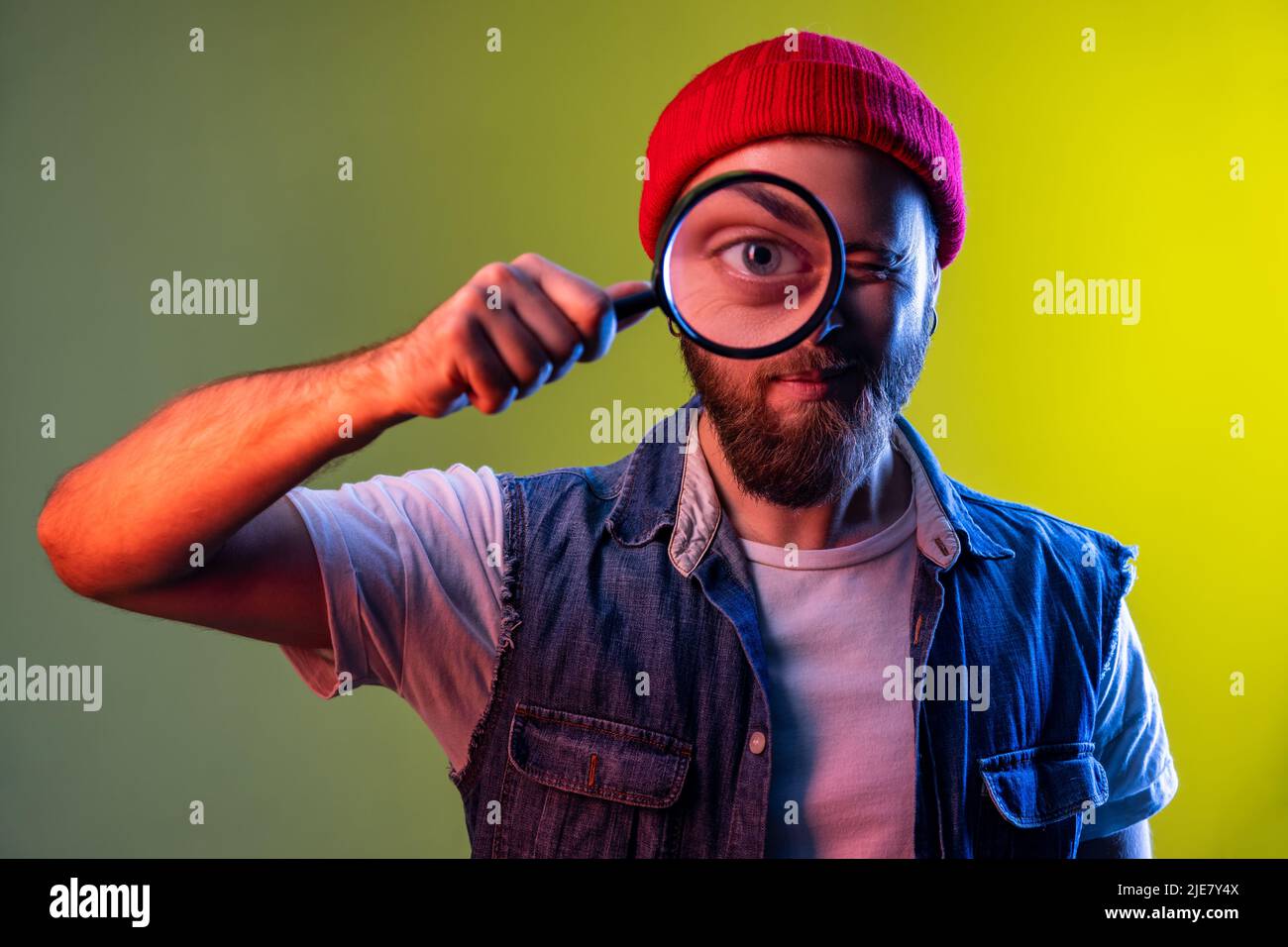 Hipster man standing, holding magnifying glass and looking at camera ...