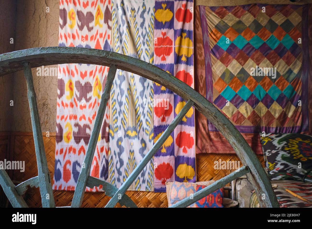 Ikat traditional silk fabric behind an old wood wheel spinner. At the ...