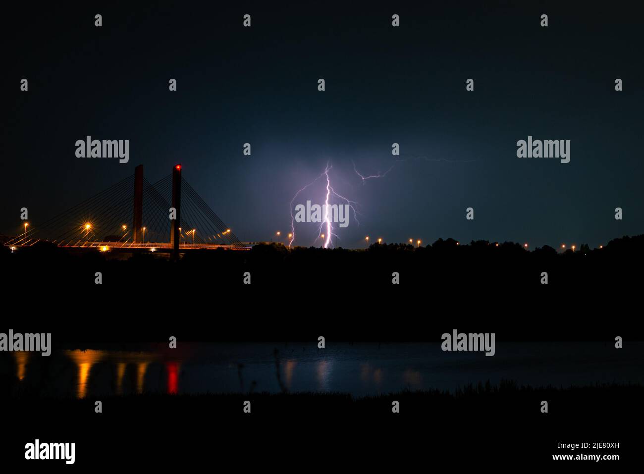 Branched lightning bolt strikes behind a cable-stayed bridge over river ...