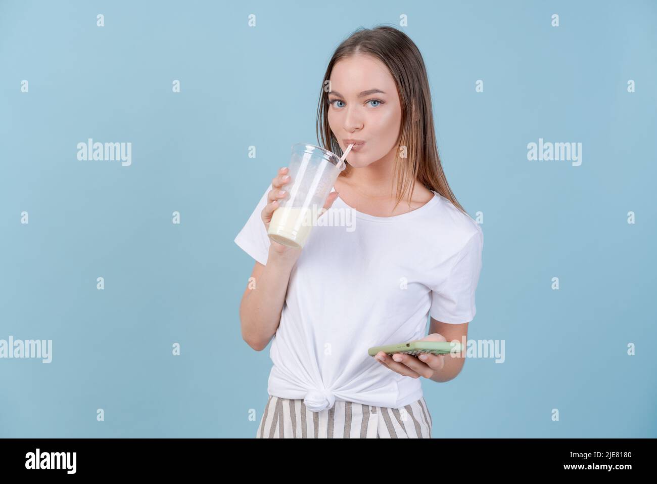 Girl stands with cocktails and smartphone on copy blue background in ...