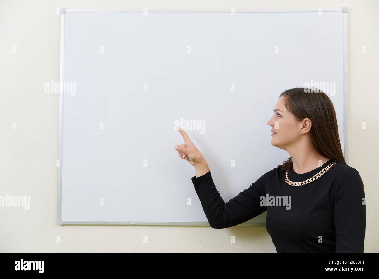 Young teacher sitting near empty white board in classroom pointing on ...