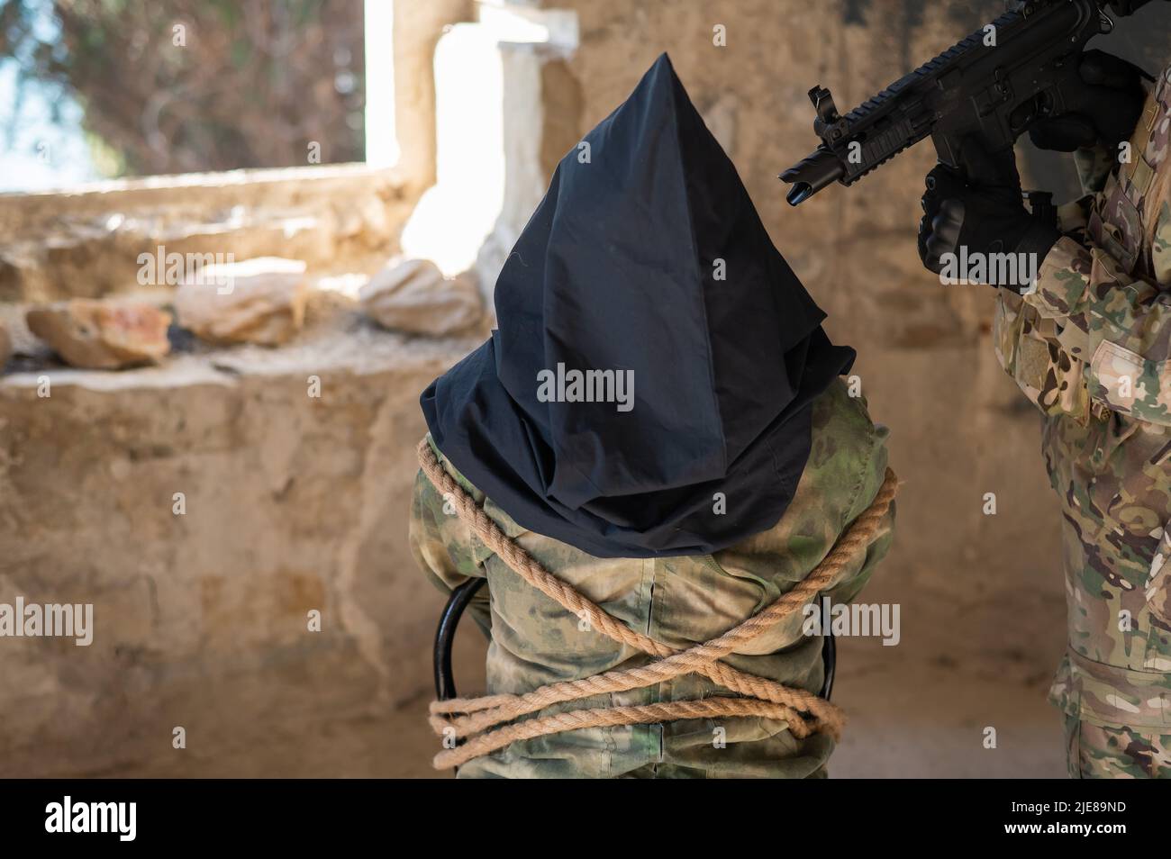 A caucasian woman in an army uniform holds a hostage with a bag on her ...