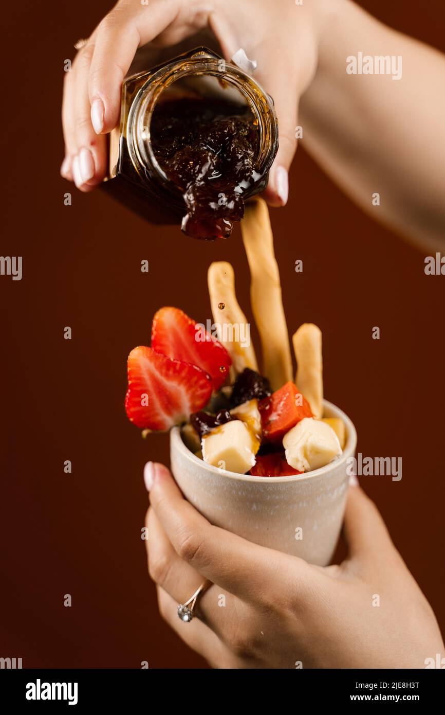 Pouring jam on mix of cheeses, grissini chopsticks and strawberry in ...