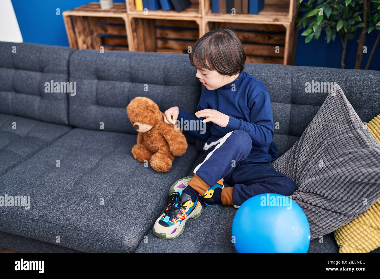 Down syndrome kid playing with teddy bear sitting on sofa at home Stock ...