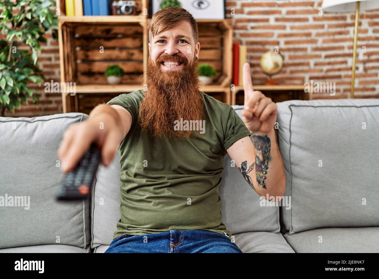 Redhead man with long beard holding television remote control smiling ...