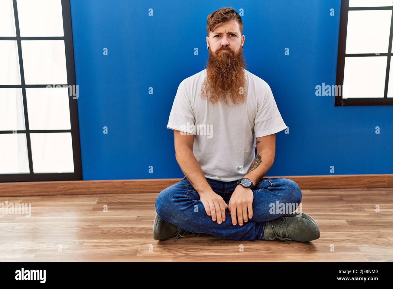 Redhead man with long beard sitting on the floor at empty room ...