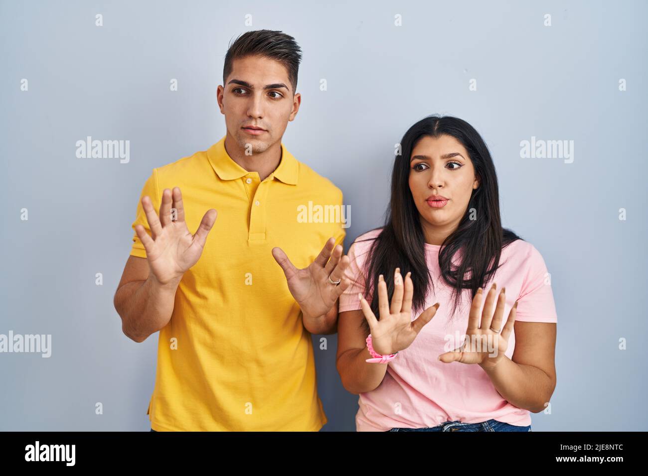 Young couple standing over isolated background moving away hands palms ...