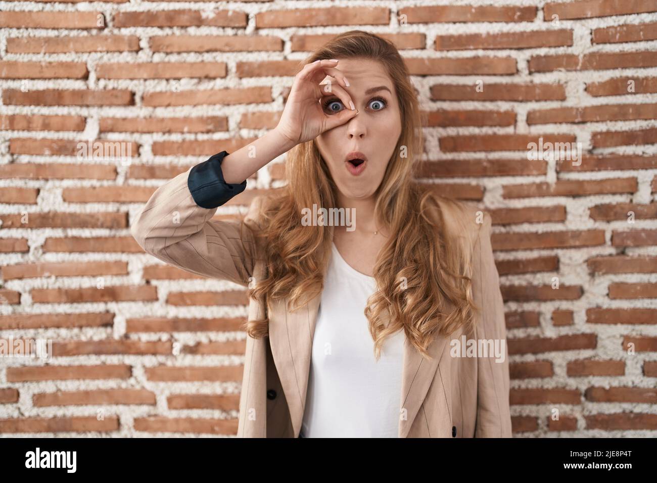 Beautiful blonde woman standing over bricks wall doing ok gesture ...