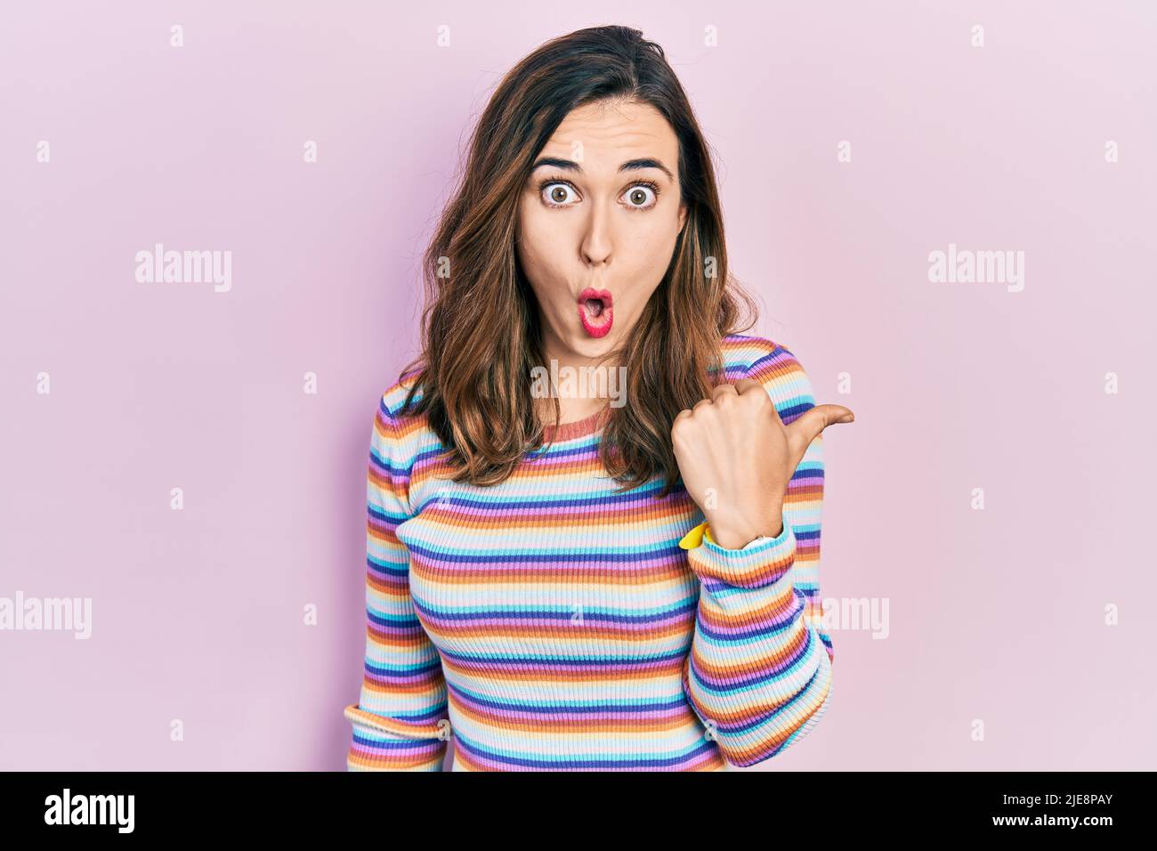 Young hispanic girl wearing casual clothes surprised pointing with hand ...