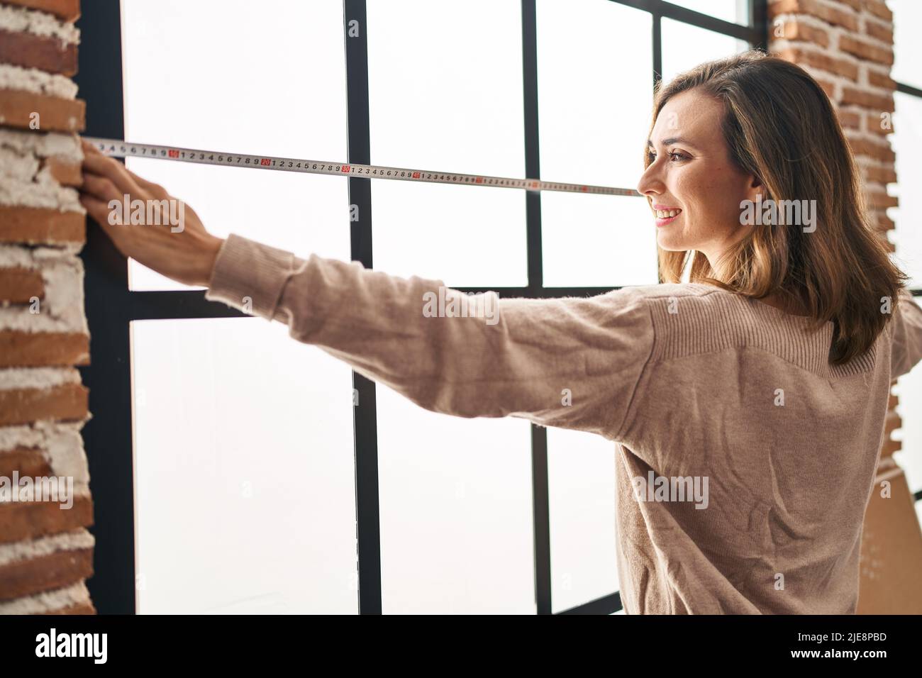 Young woman smiling confident measuring window at new home Stock Photo ...