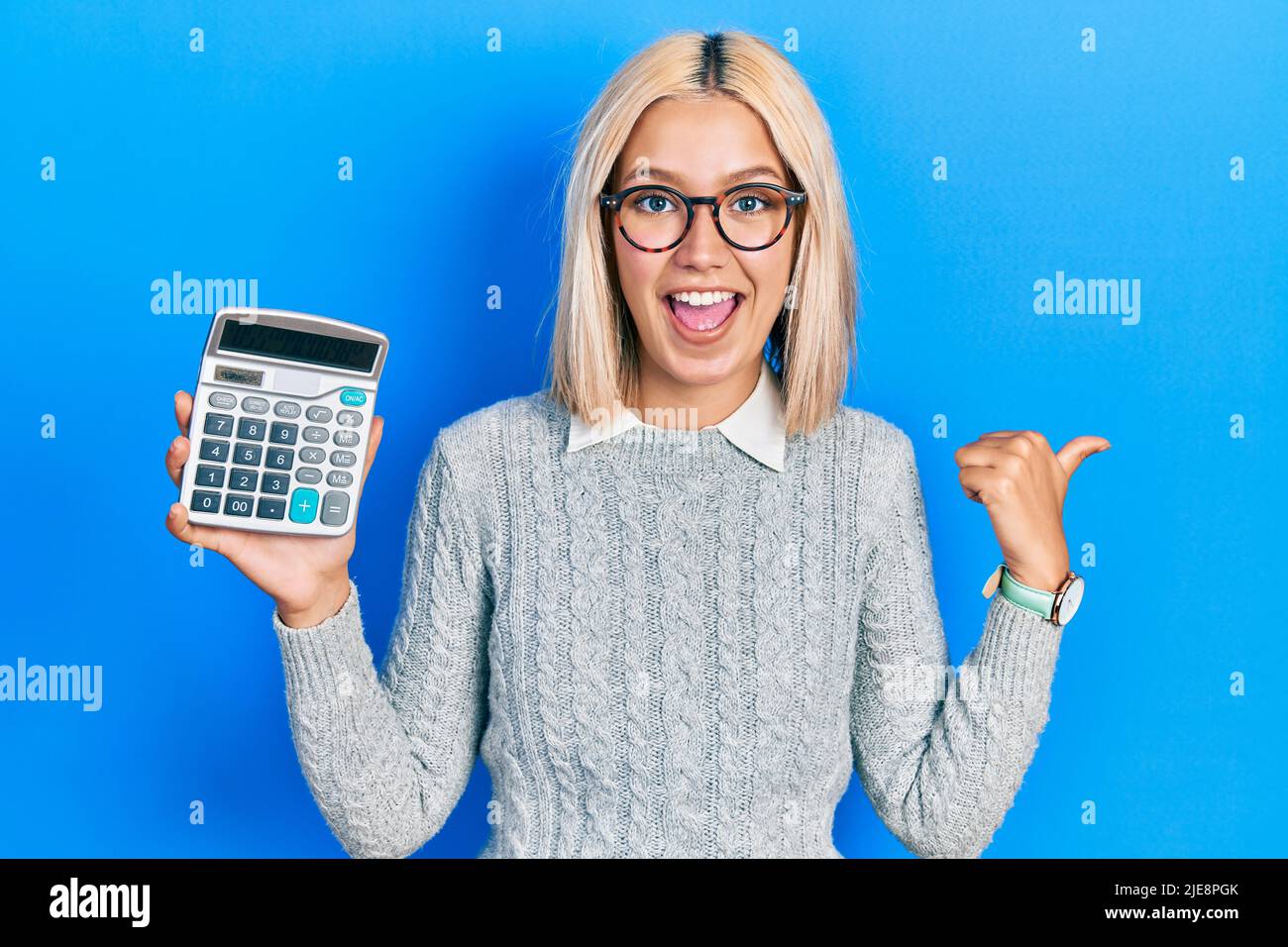 Beautiful blonde woman showing calculator device pointing thumb up to ...