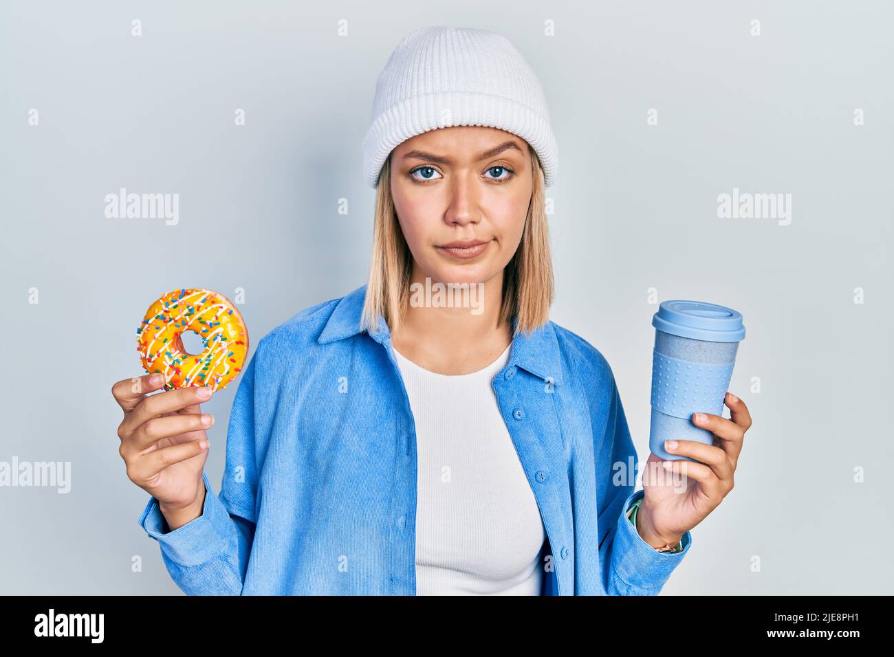 Beautiful blonde woman eating doughnut and drinking coffee skeptic and ...