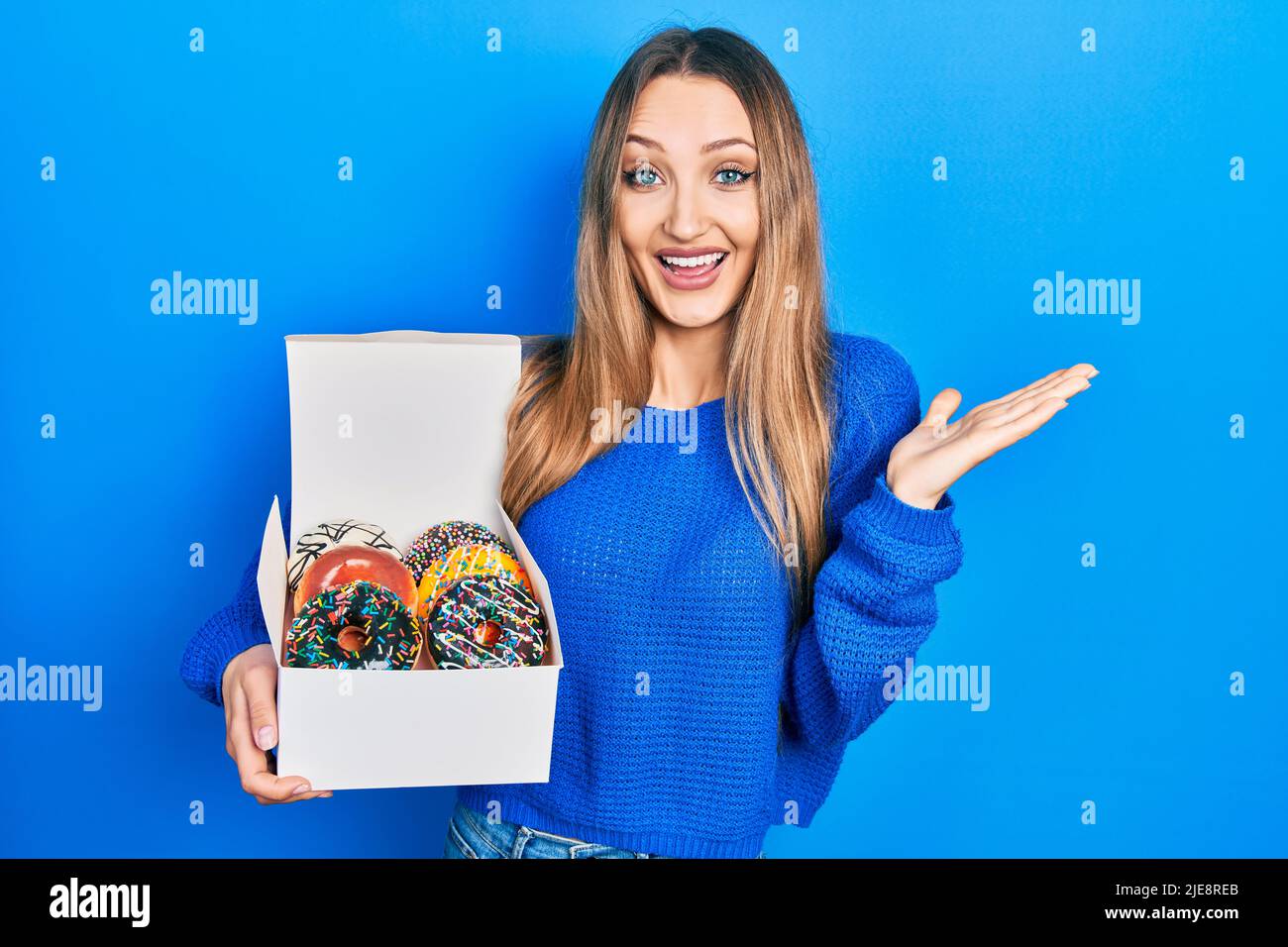 Young blonde girl holding box of tasty colorful doughnuts celebrating ...