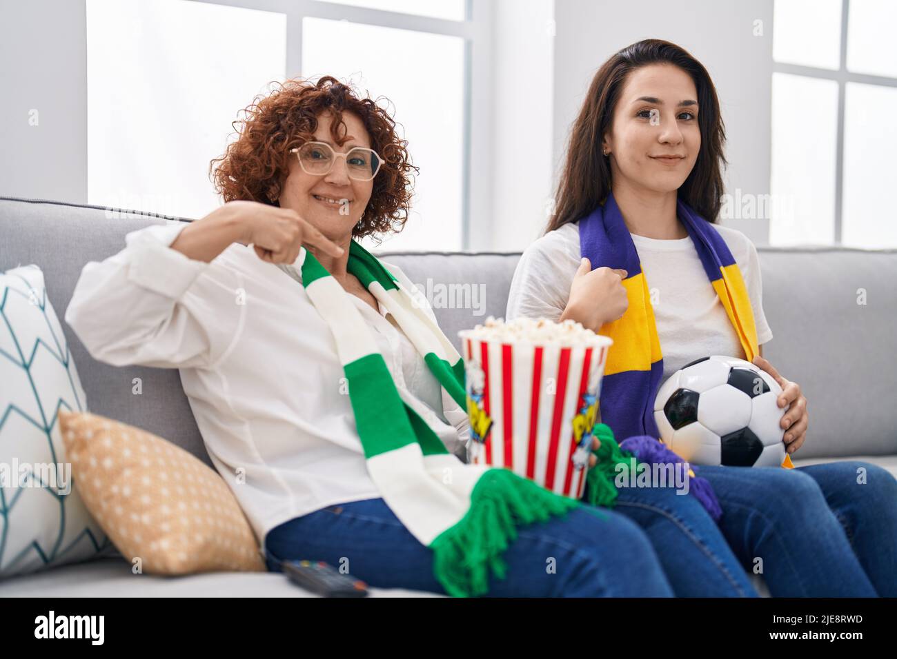 Hispanic mother and daughter watching football supporting team pointing ...
