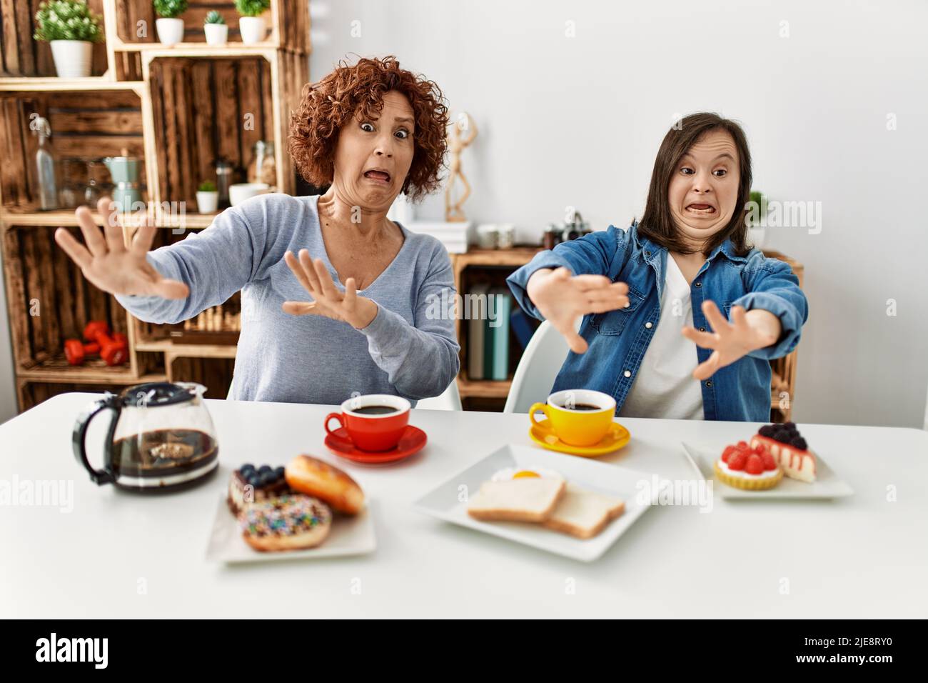 Family of mother and down syndrome daughter sitting at home eating breakfast afraid and ...