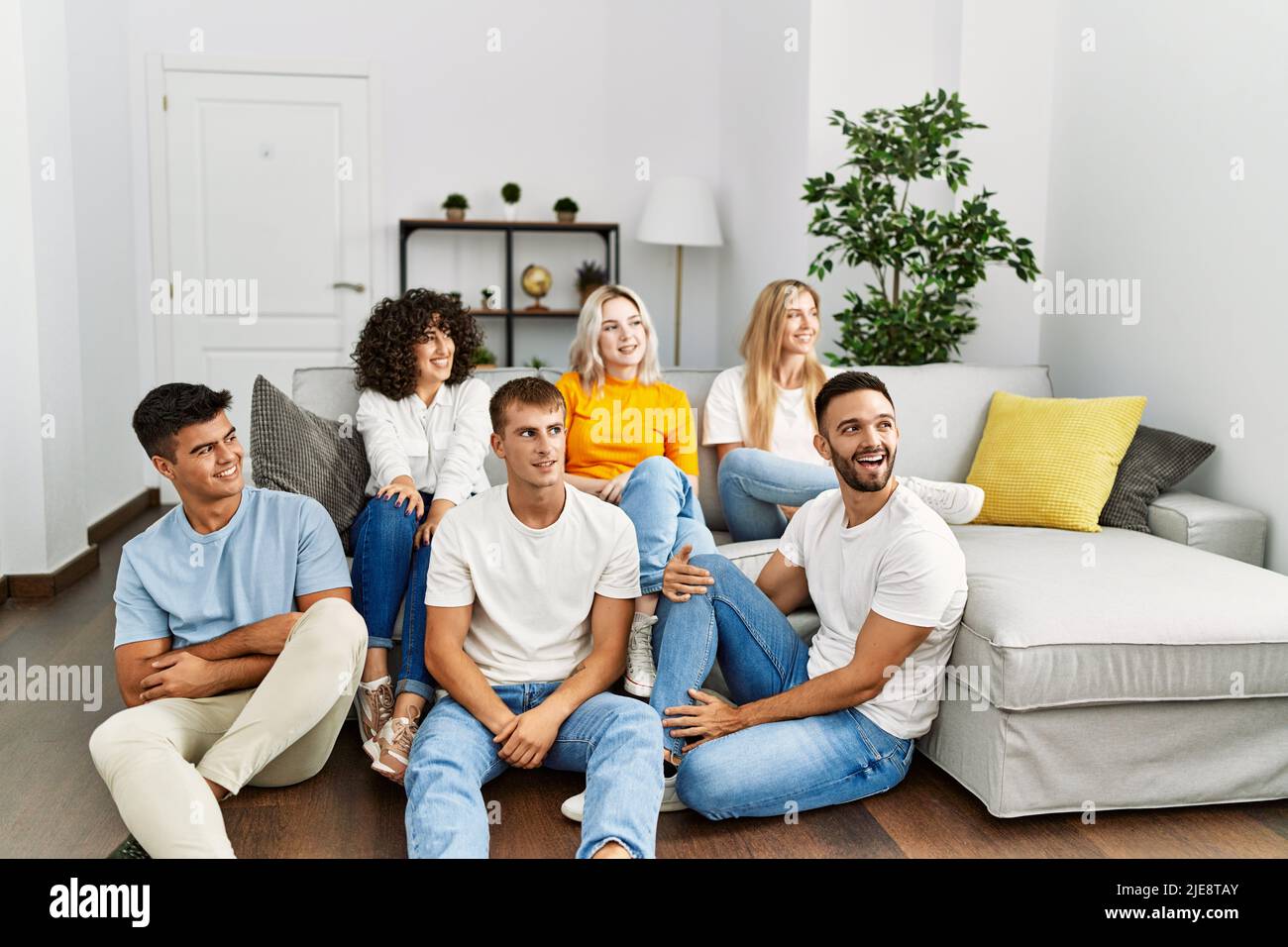 Group of people sitting on the sofa and floor at home looking away to ...