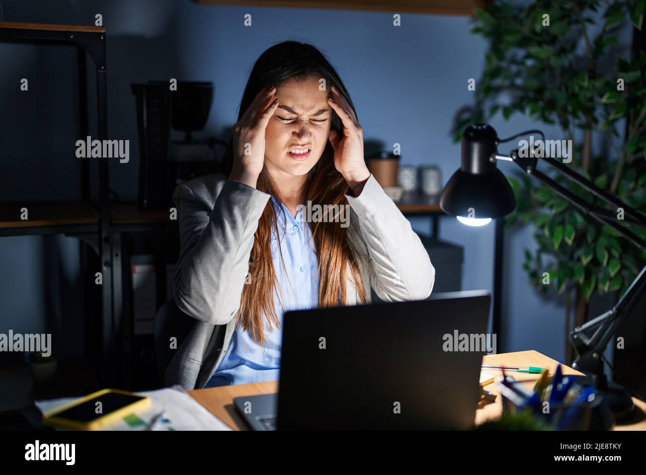 Young brunette woman working at the office at night with hand on head ...