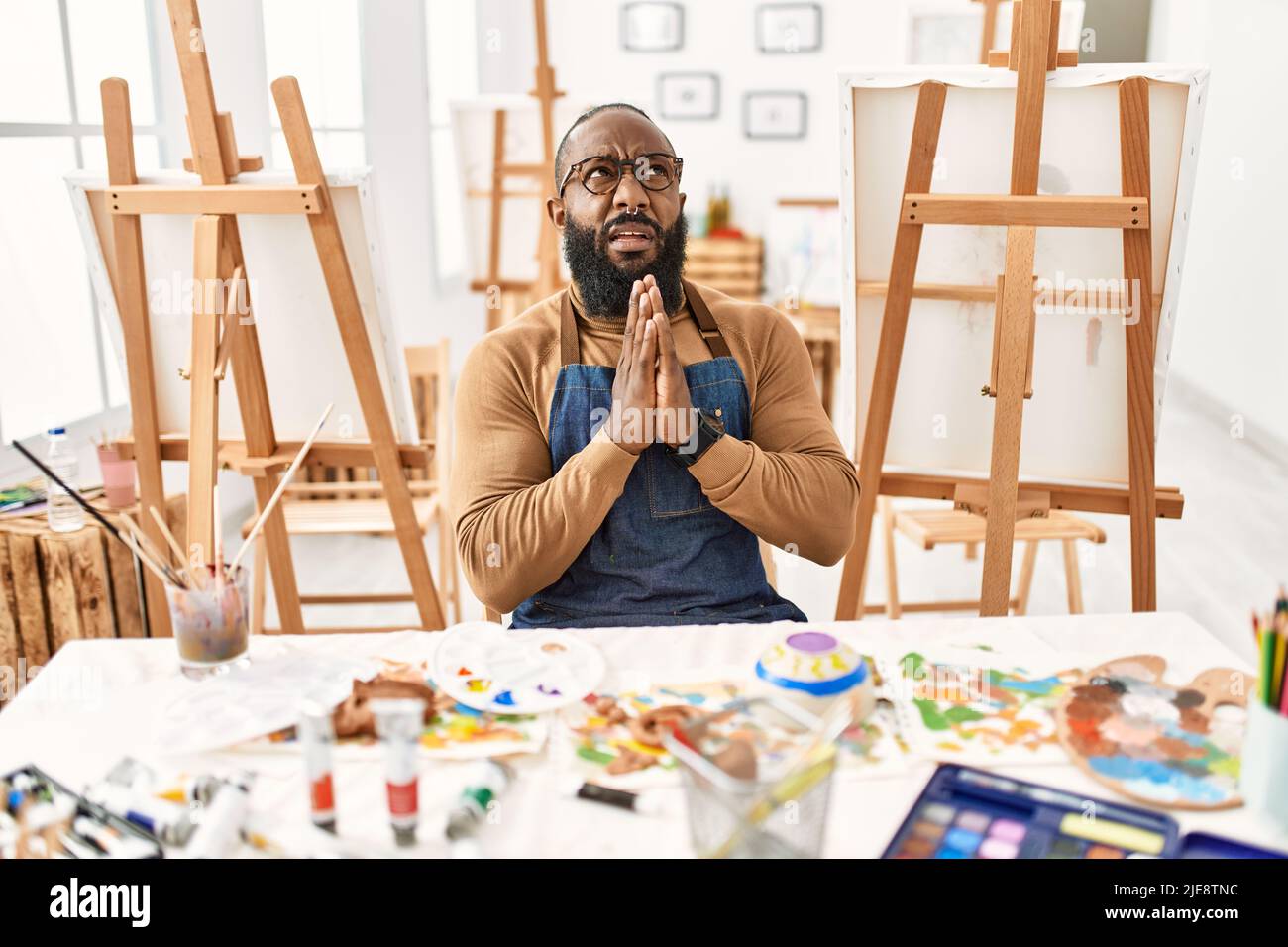 African american artist man at art studio begging and praying with ...
