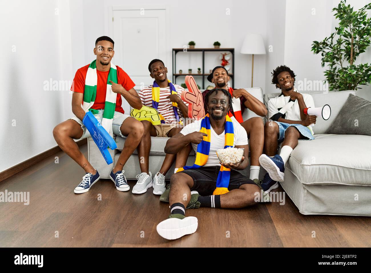 Young african men wearing team scarf cheering football game pointing ...