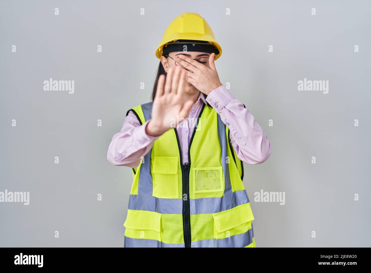 Hispanic girl wearing builder uniform and hardhat covering eyes with ...