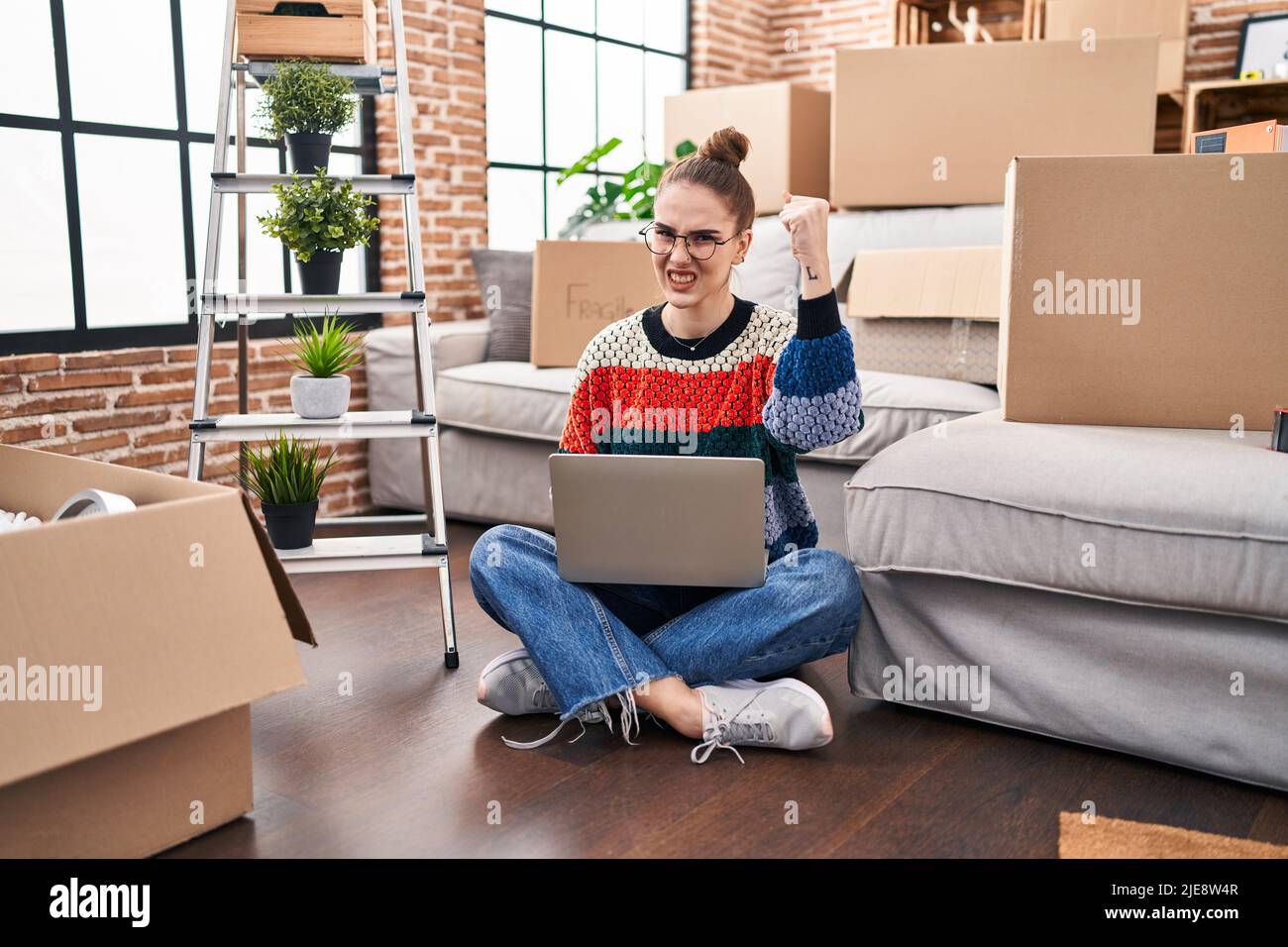 Young hispanic girl sitting on the floor at new home with laptop ...
