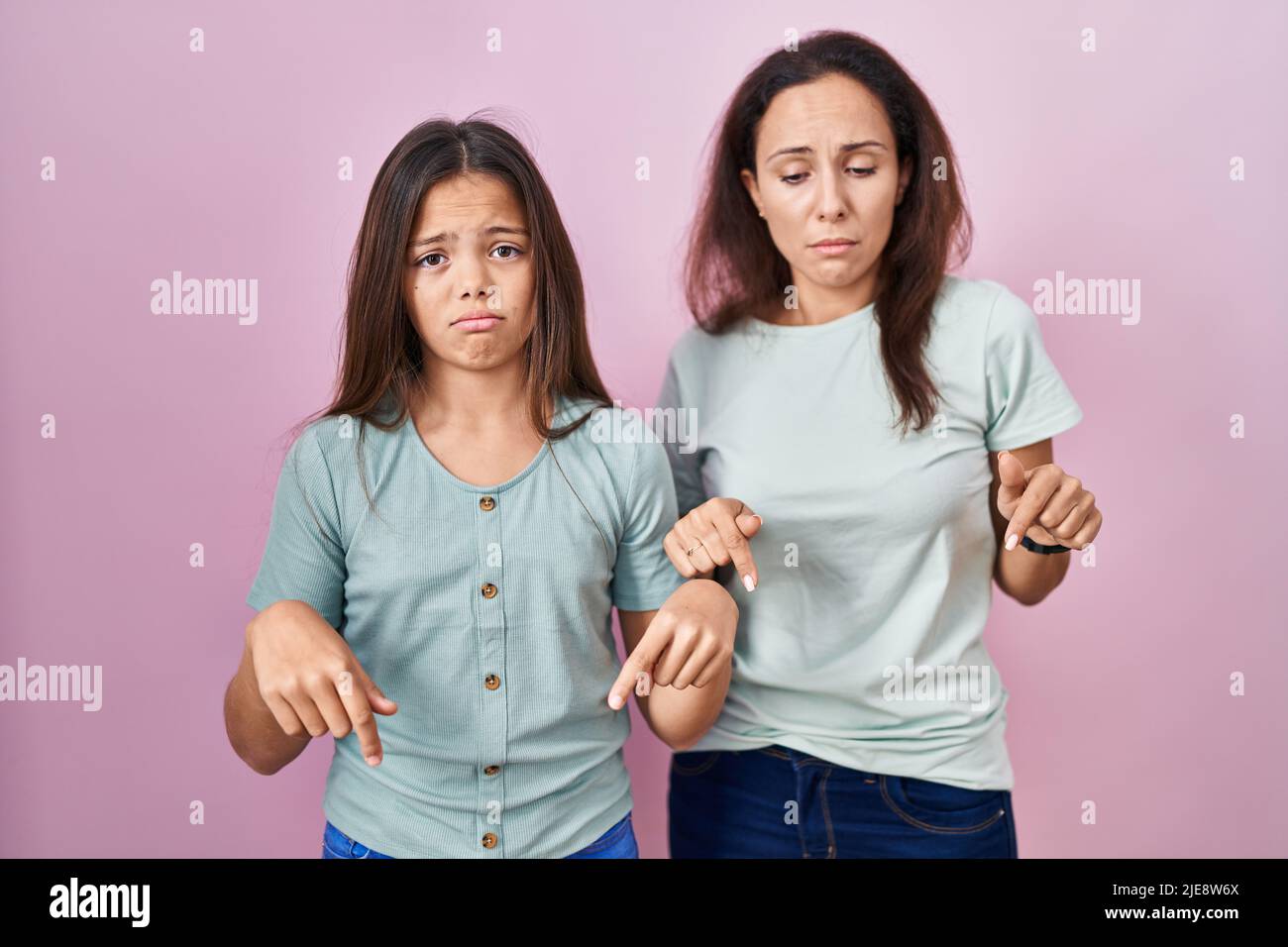Young Mother And Daughter Standing Over Pink Background Pointing Down