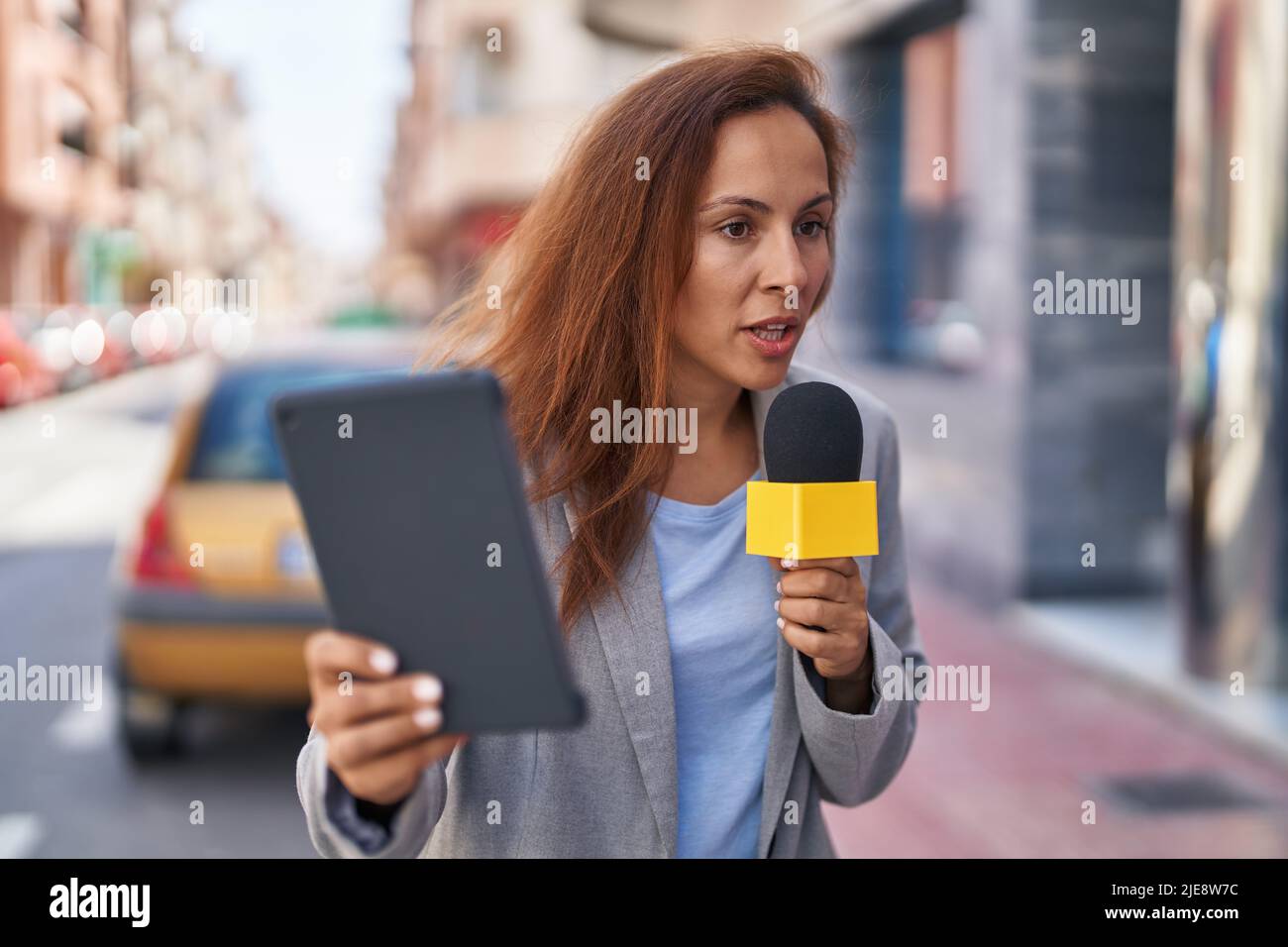 Young woman reporter working using microphone and touchpad at street ...