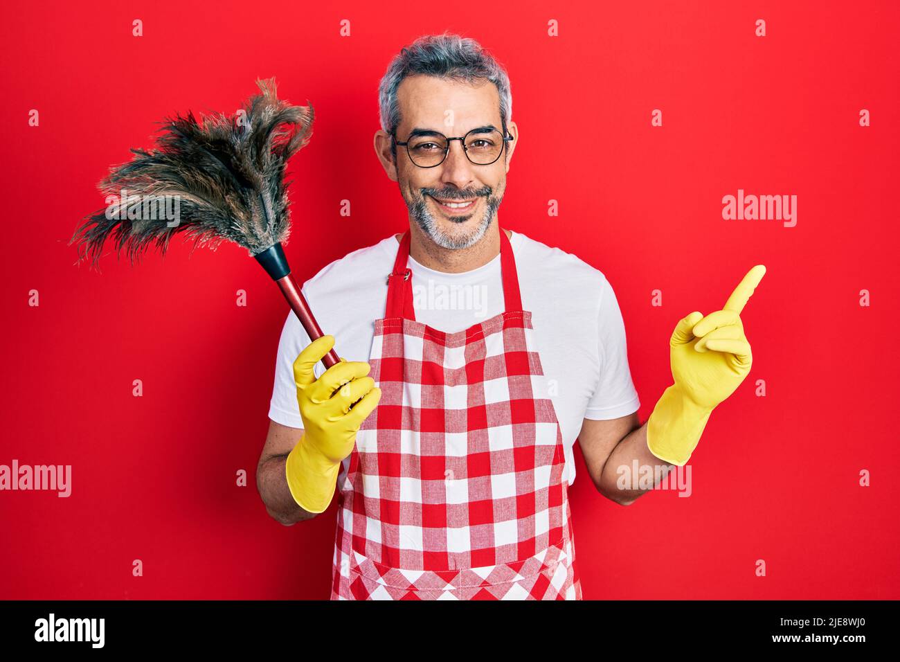 Handsome middle age man with grey hair wearing apron holding cleaning ...