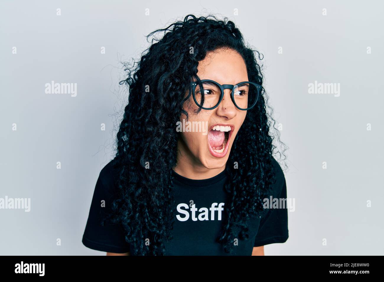 Young hispanic woman with curly hair wearing staff t shirt angry and ...