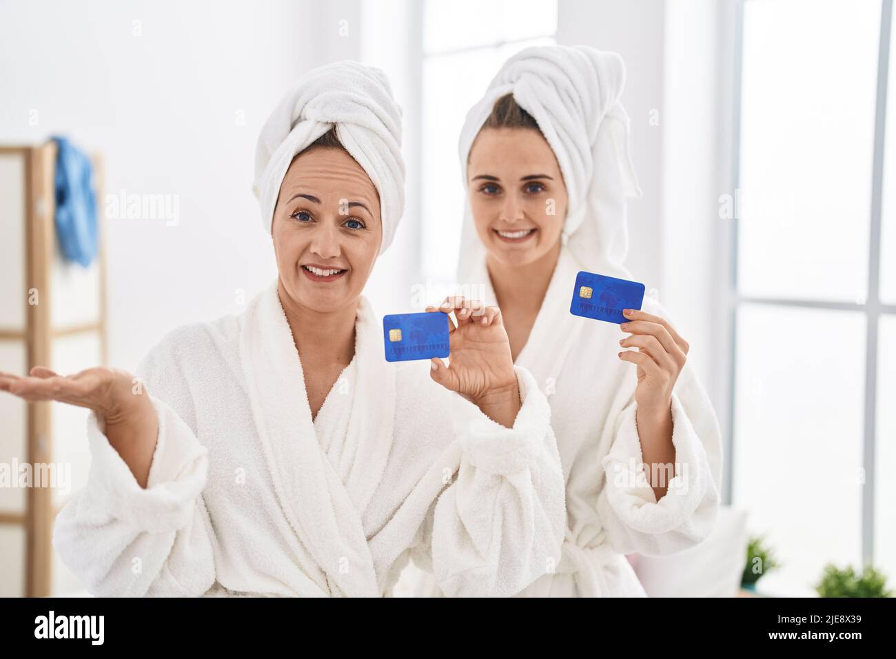 Middle age woman and daughter wearing bathrobe holding credit card ...