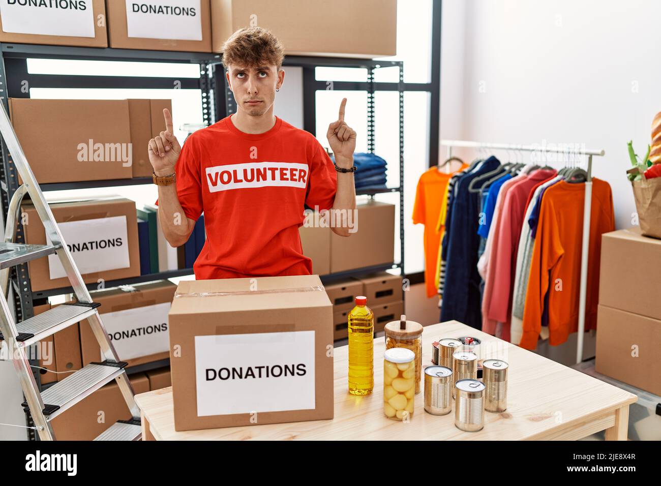 Young caucasian man volunteer holding donations box pointing up looking ...