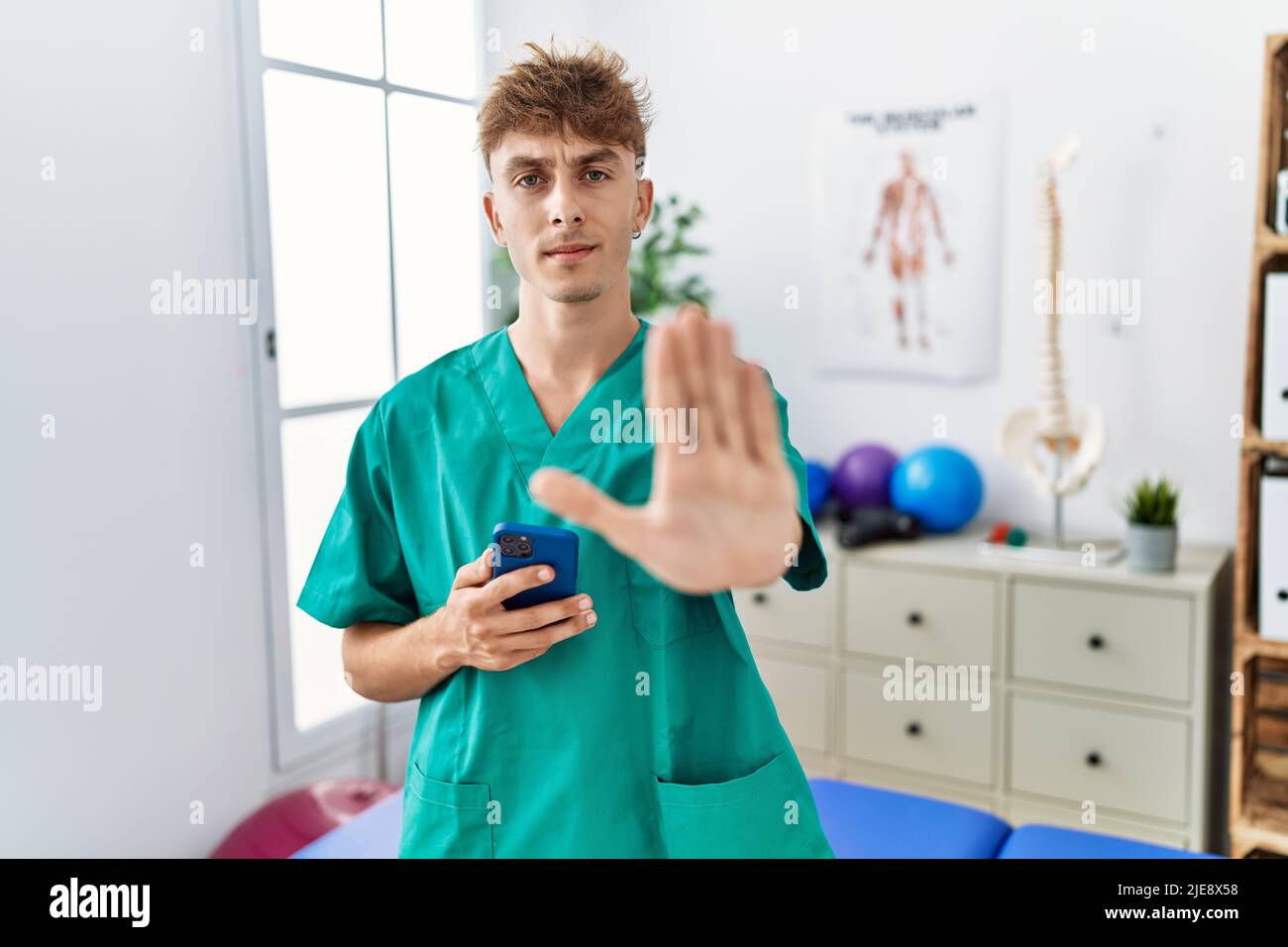 Young caucasian physio man using smartphone at medical clinic with open ...