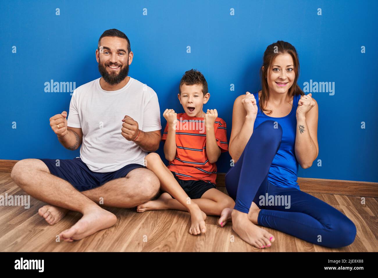 Family of three sitting on the floor at home celebrating surprised and ...