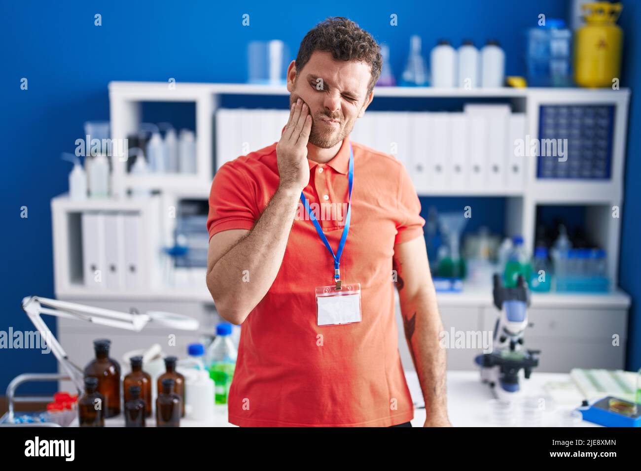 Young hispanic man working at scientist laboratory touching mouth with ...